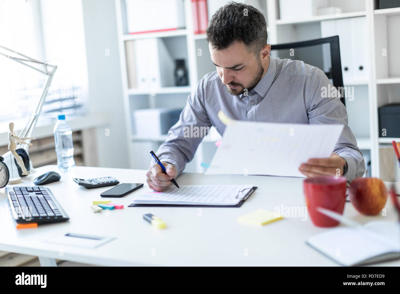 Ein junger Mann im Büro sitzt an einem Tisch, hält einen Stift in der ... Ein junger Mann im Büro sitzt an einem Tisch, hält einen Stift in der ...