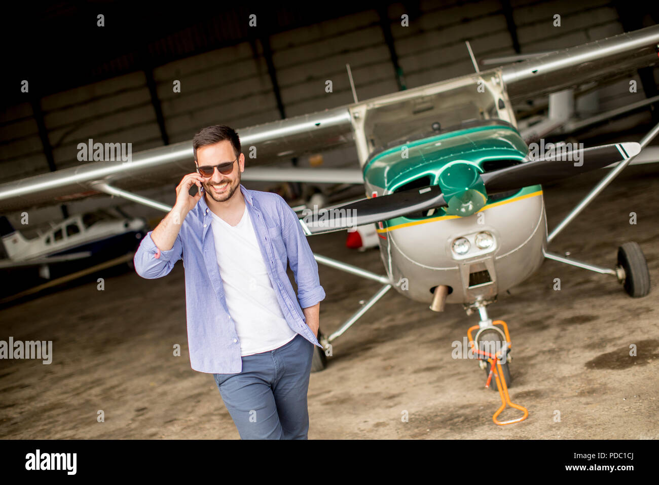 Junge hübscher junger Pilot Kontrolle Flugzeug im Hangar und mit Handy ...