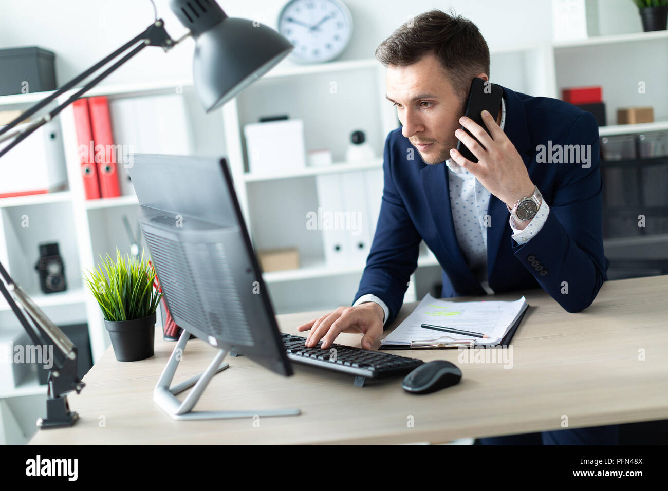 Ein junger Mann steht in der Nähe von einem Tisch im Büro, am Telefon ...