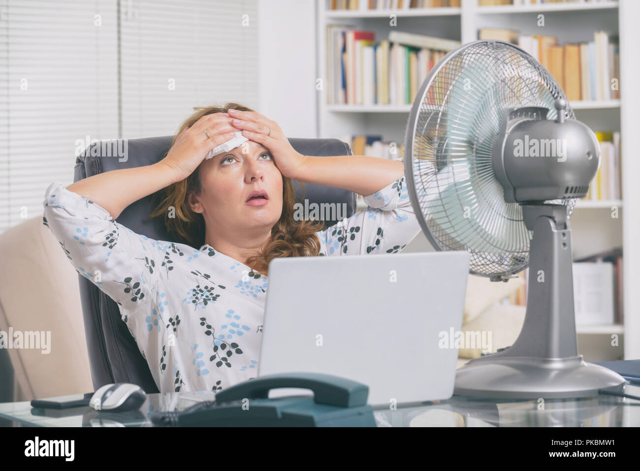 Frau leidet unter der Hitze, während der Arbeit im Büro und versucht ...