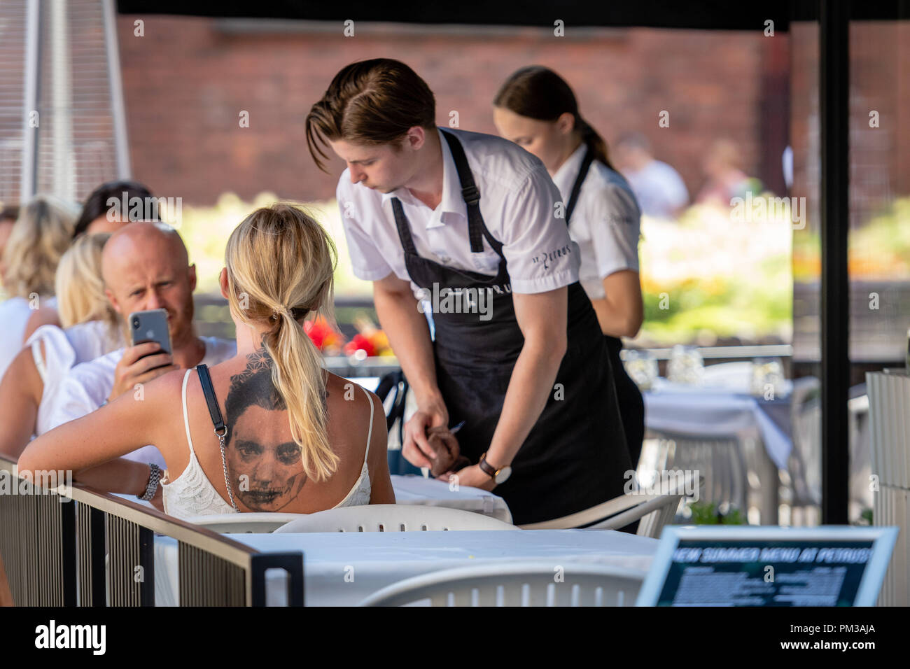 RIGA, Lettland - 31. JULI 2018: Café im Freien am Tisch sitzt eine Frau mit einem großen Tattoo ...