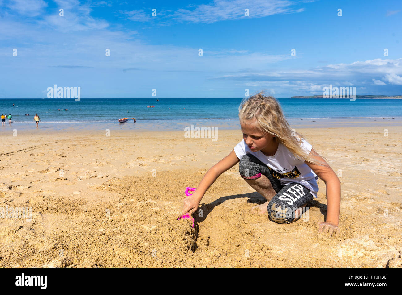 Eine hübsche kleine blonde Mädchen graben ein Loch am Strand mit einem ...