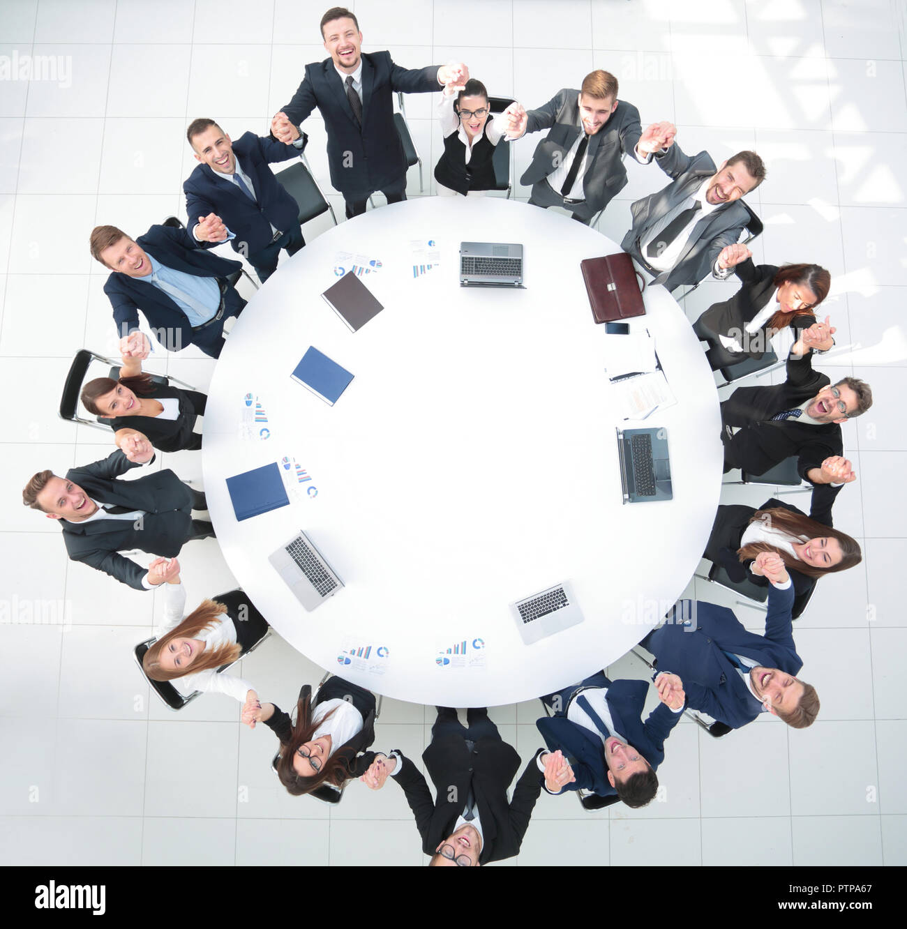 Große Unternehmen Team am runden Tisch sitzen und hob seine Hände hoch ...