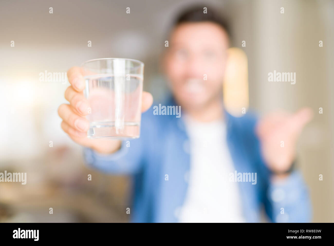 Jungen gutaussehenden Mann trinkt ein Glas Wasser zu Hause zeigen und ...