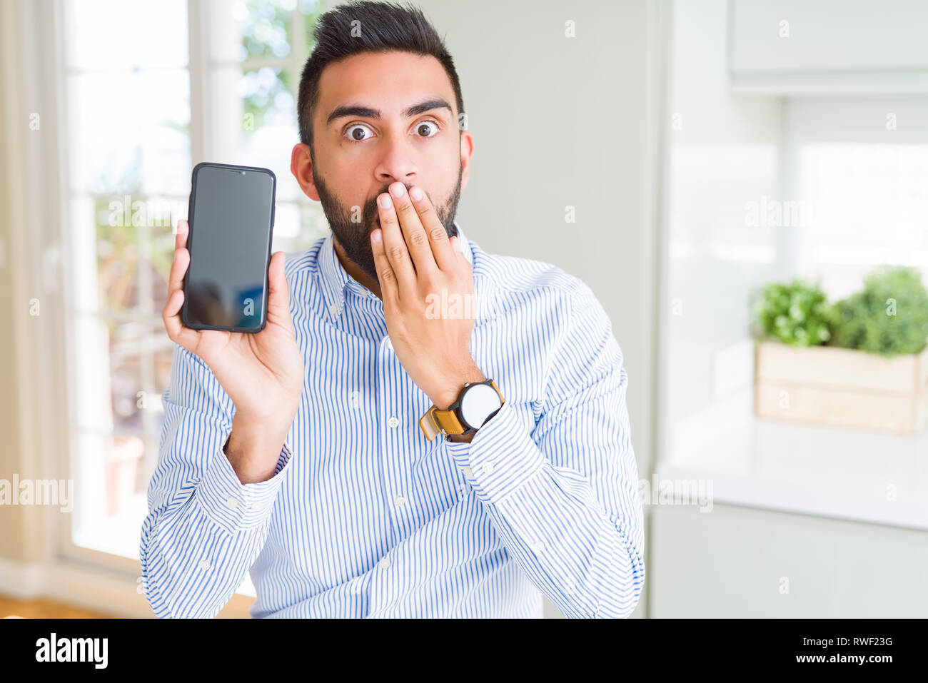 Stattliche Hispanic Mann zeigt der Bildschirm des Smartphones decken den Mund mit der Hand mit ...