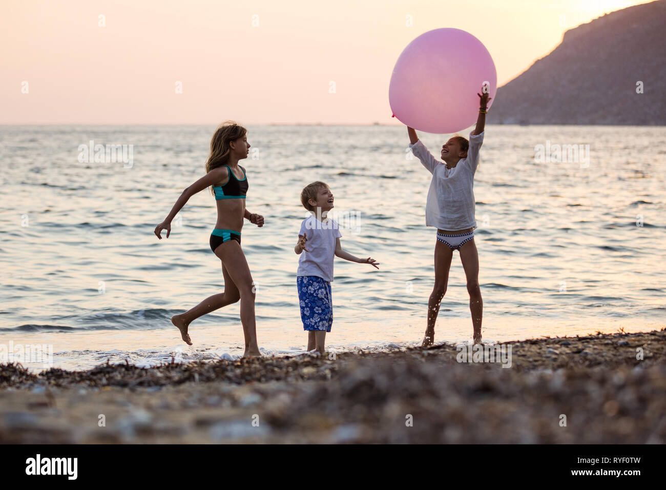 Drei Kinder beim Spielen mit riesigen rosa Ballons am Strand bei ...