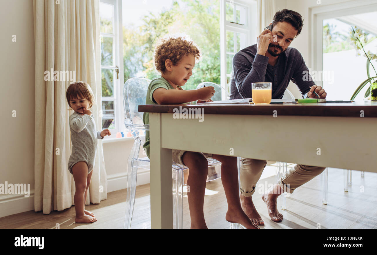 Mann sitzt an einem Tisch und reden über Mobiltelefon mit Kindern in ...