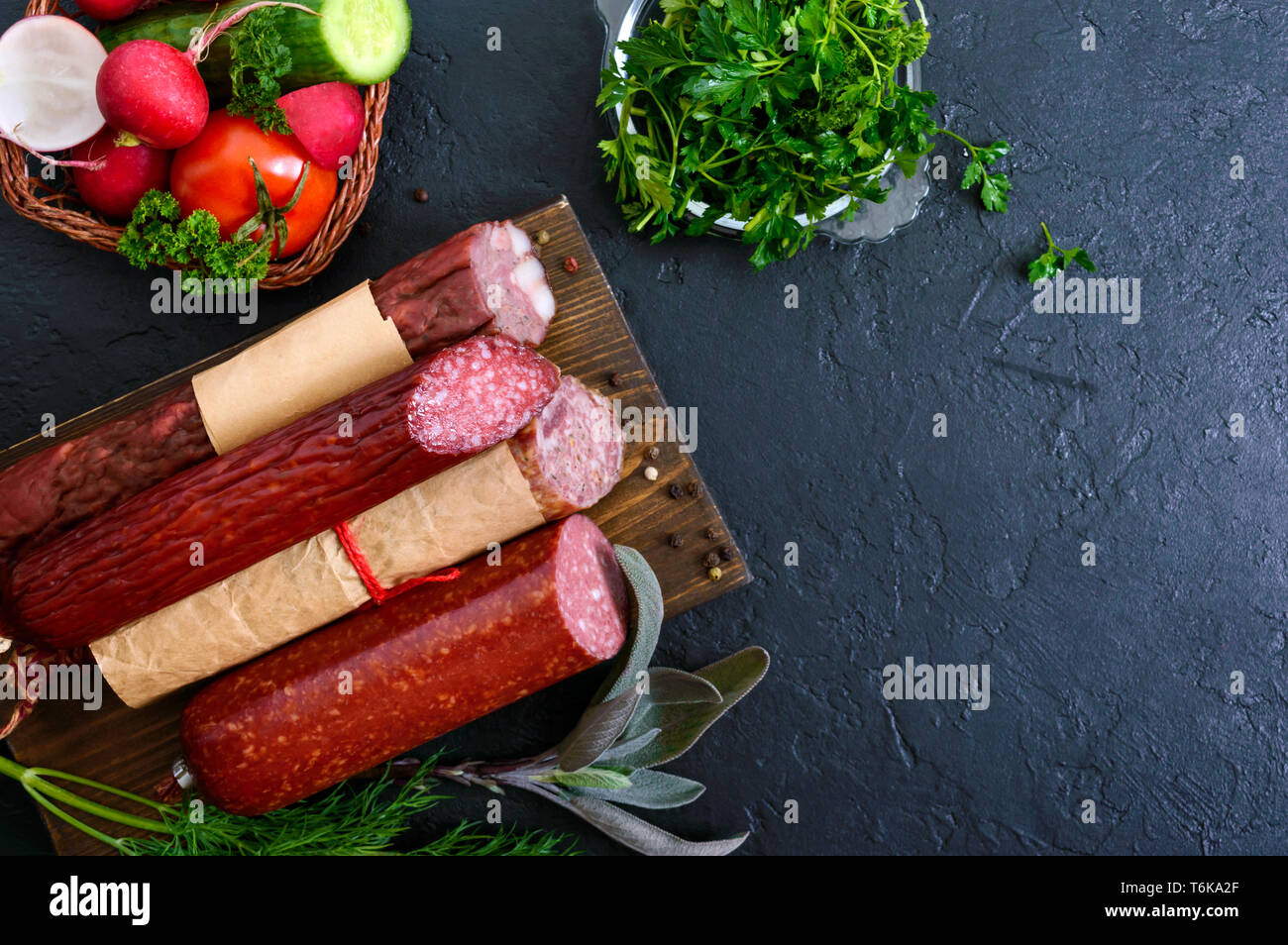 Mehrere Arten von Wurst, frisches Gemüse und Grüns auf einem schwarzen ...