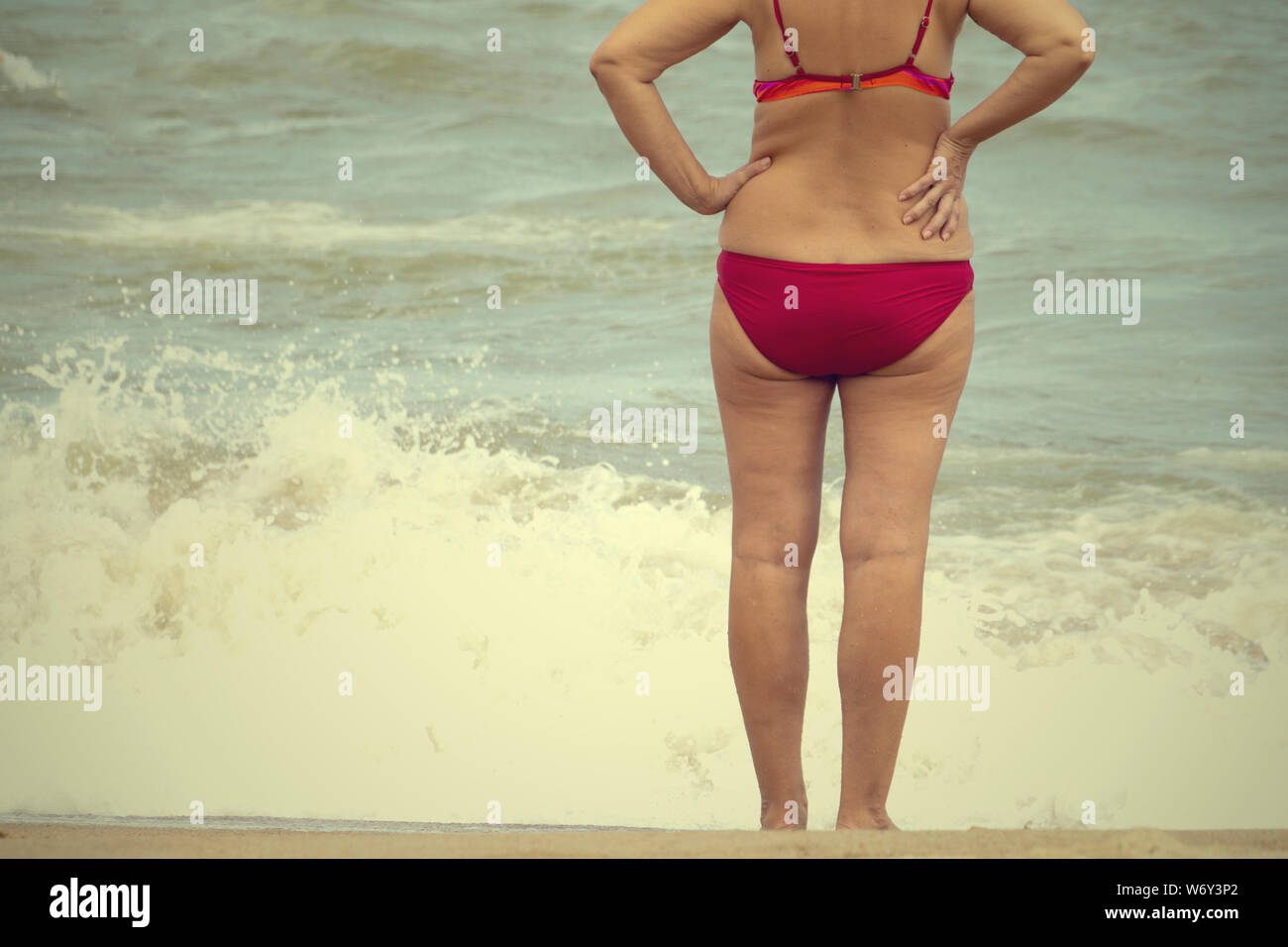 Weibliche Gesäß wird mit Fett abgedeckt. Cellulite. Frau im Badeanzug Spaziergänge in den Sand ...