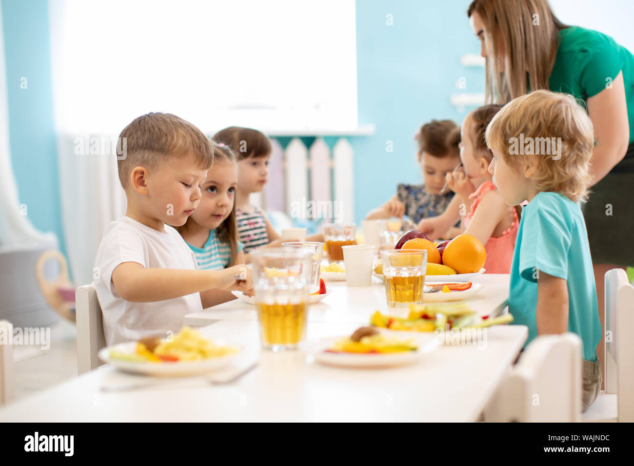 Kinder haben ein Abendessen im Kindergarten. Kleine Jungen und Mädchen ...