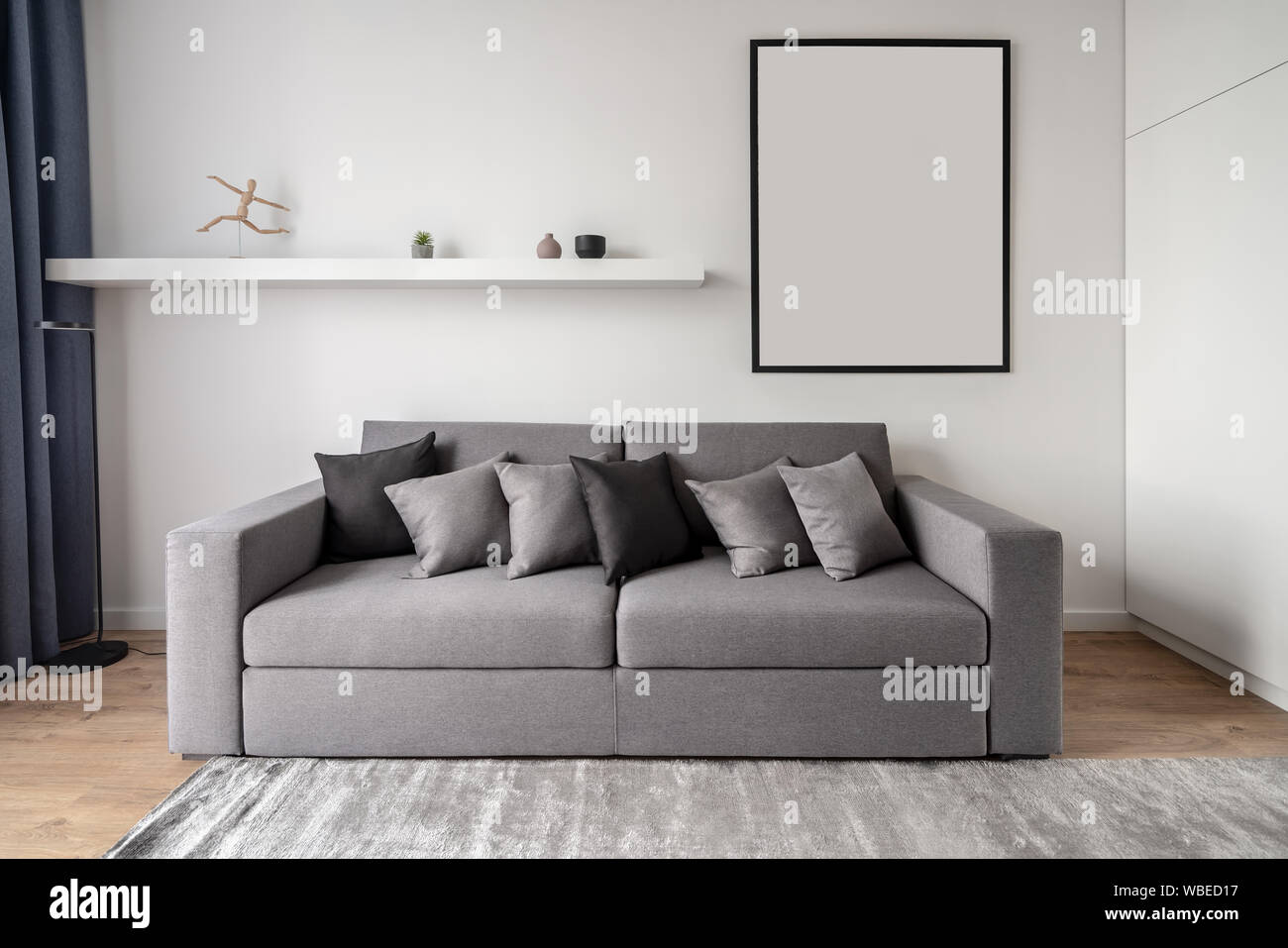 Einrichtung in einem modernen Stil mit weiBen Wanden und einem Parkettboden mit einem Teppich auf dem Boden. Es ist ein graues Sofa mit Kissen Regal mit Dekorationen schwarz Stockfotografie Alamy