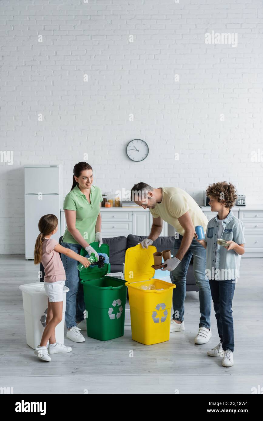 Alegre familia clasificando basura en latas con emblema de reciclaje en ...
