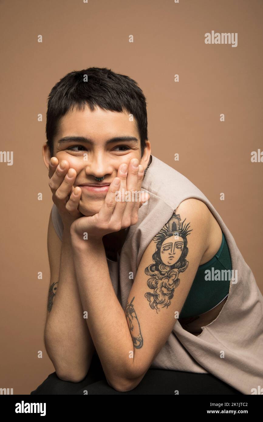 Retrato De Un Hombre Feliz Y Joven No Binario Con Tatuajes Y Cabeza En Las Manos Fotografía De