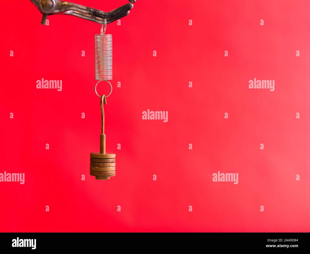 Masses accrochée à un ressort étiré isolé sur un fond rouge. Expérience ...