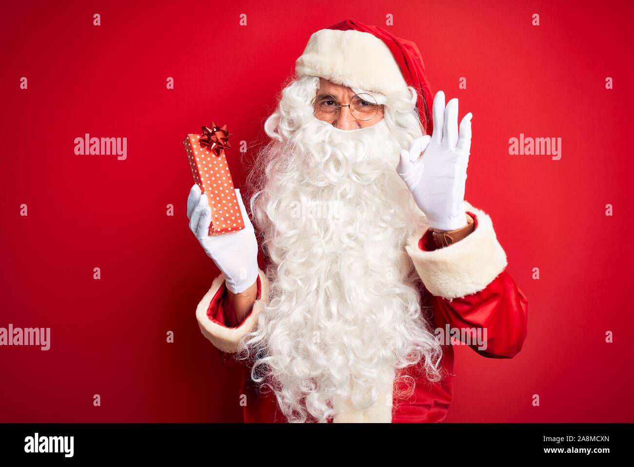 L'âge moyen homme portant costume père noël holding don sur fond rouge ...