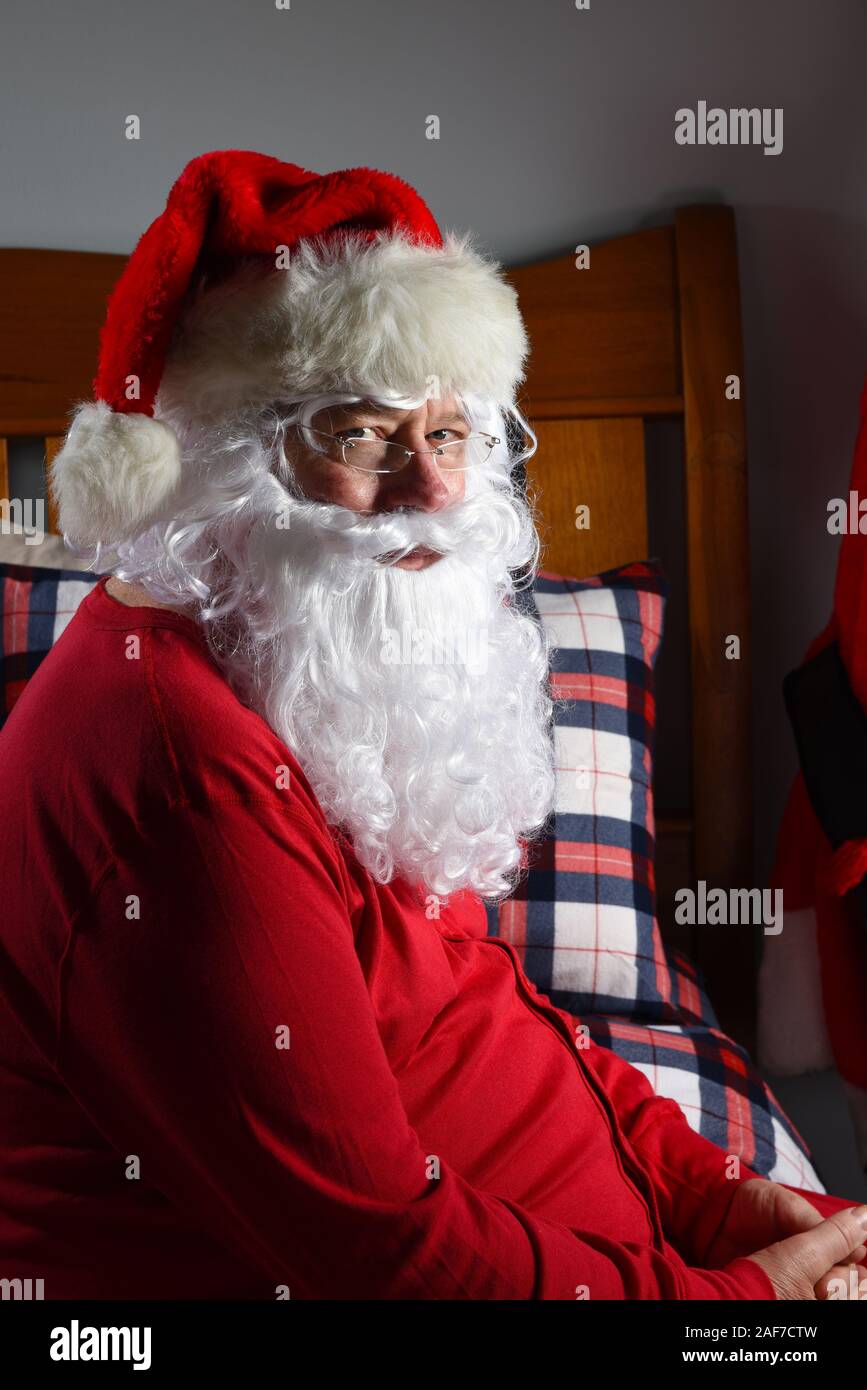 Gros plan du Père Noël assis sur son lit dans sa red long Johns, prêt à ...