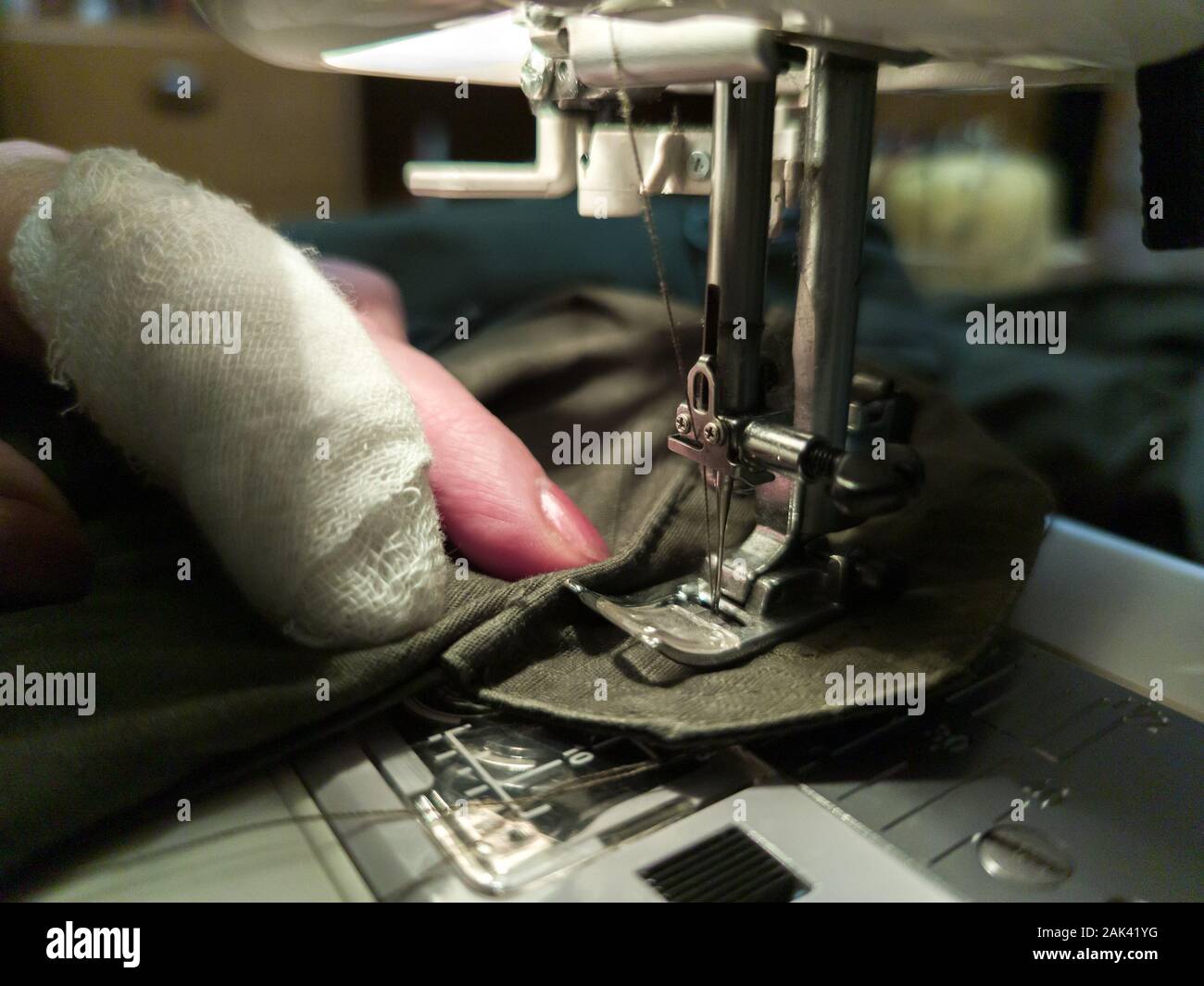 Une main de femme de avec un doigt bandé coud avec une machine à coudre ...