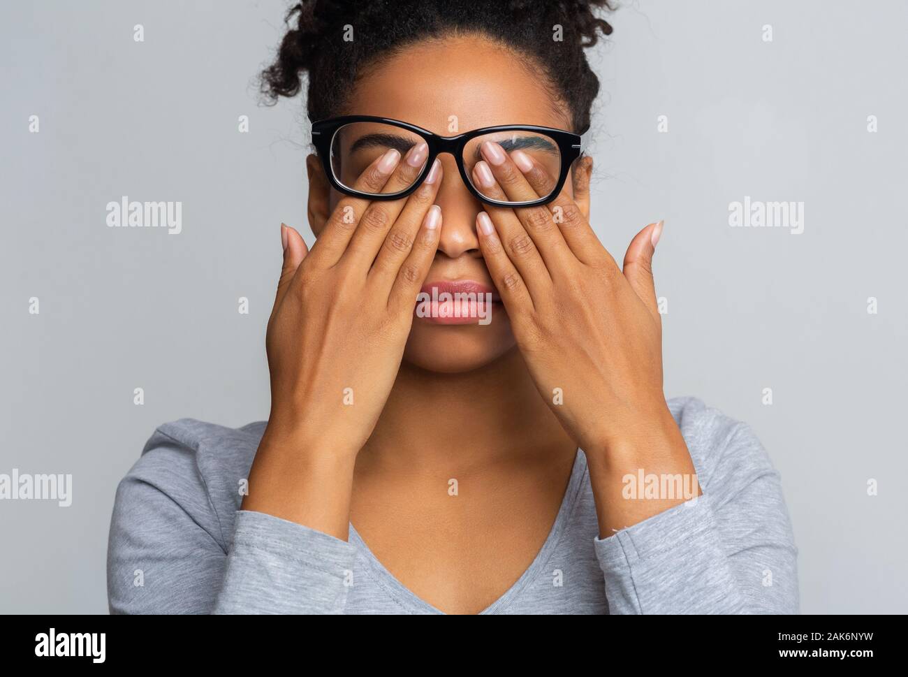 Petite fille africaine dans les verres frotte ses yeux, souffrant de ...