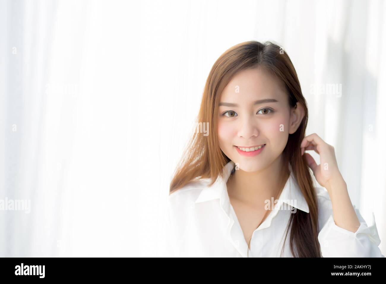 Portrait of beautiful young asian woman standing la fenêtre et sourire ...