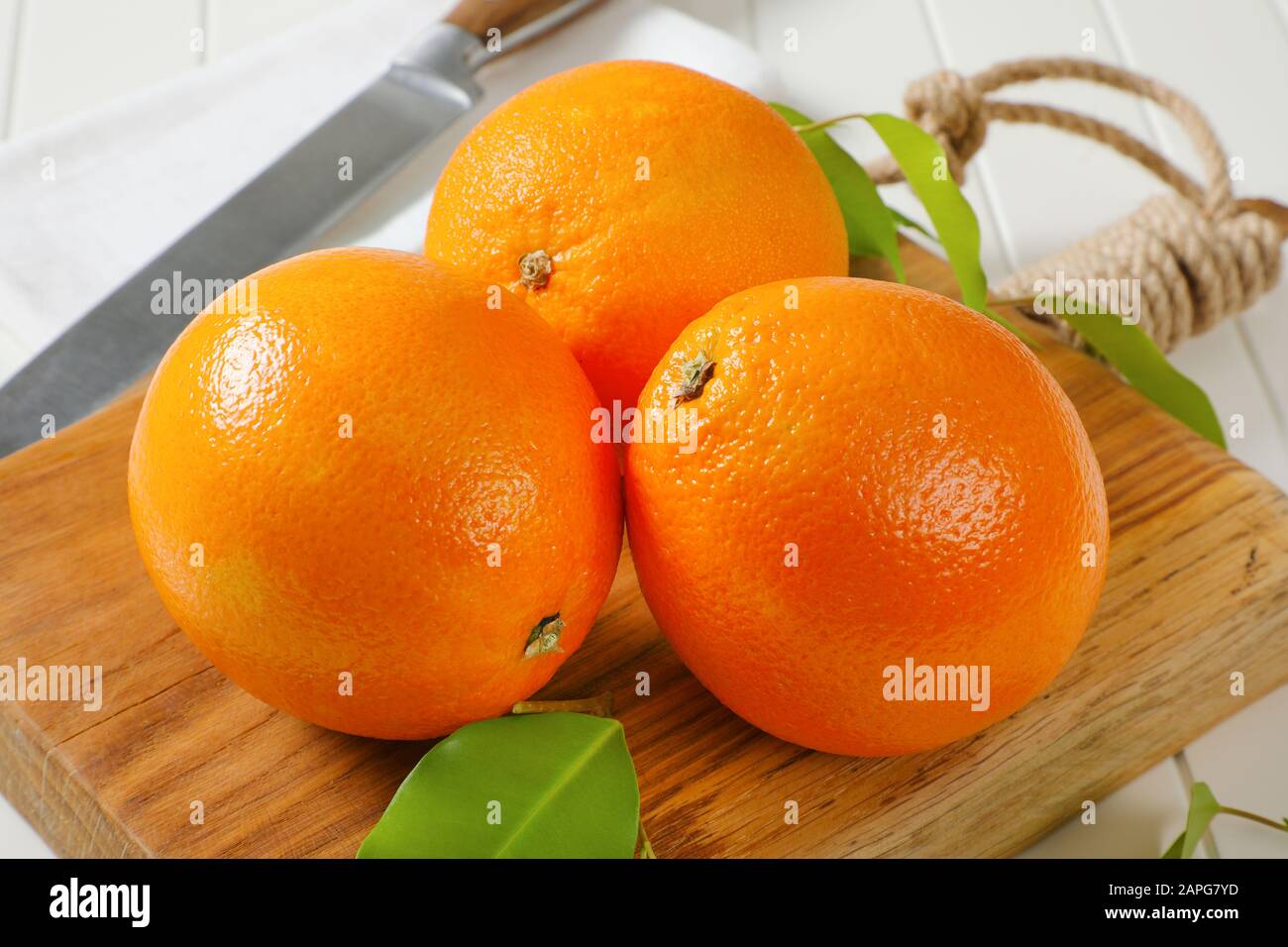 Trois oranges et feuilles entières mûres sur le tableau de découpe ...