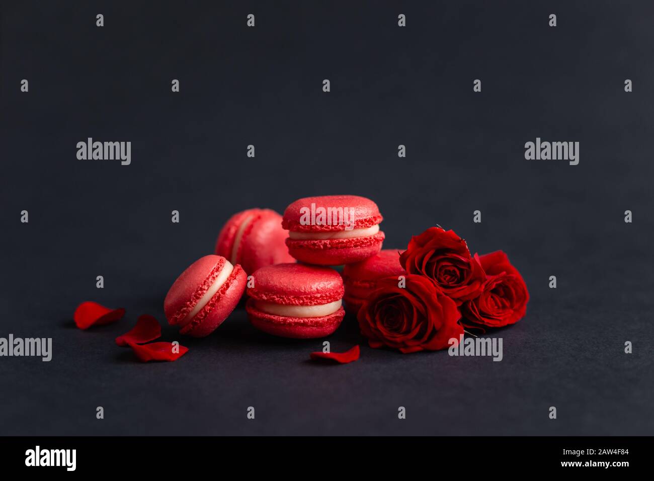 Délicieux macarons français avec des roses rouges sur fond noir ...