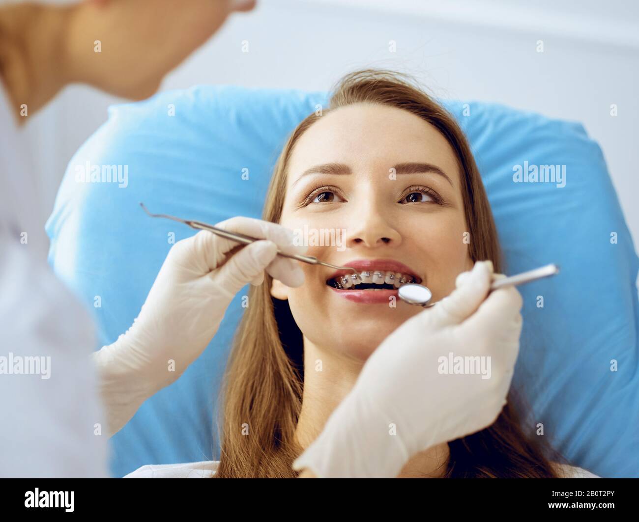 Souriante jeune femme avec boîtiers orthodontiques examiné par dentiste de clinique dentaire. La ...