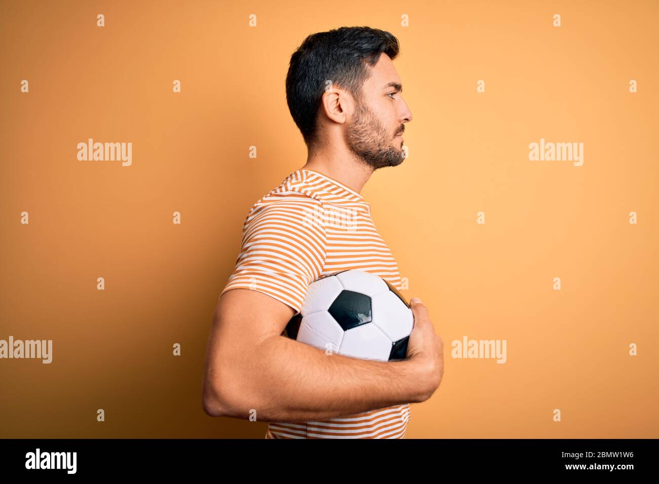 Beau joueur avec barbe jouant au football tenant le ballon de football ...