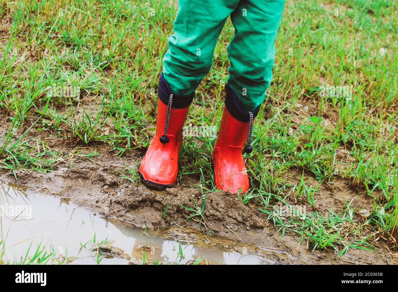 Enfant avec des bottes rouges jouant et sautant dans la boue flaque ...