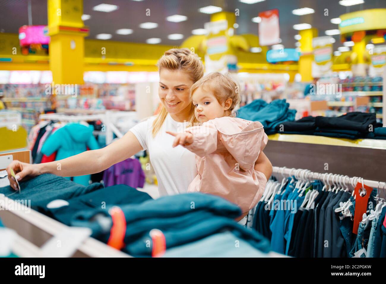 Mère avec sa petite fille qui choisit des vêtements dans le magasin ...
