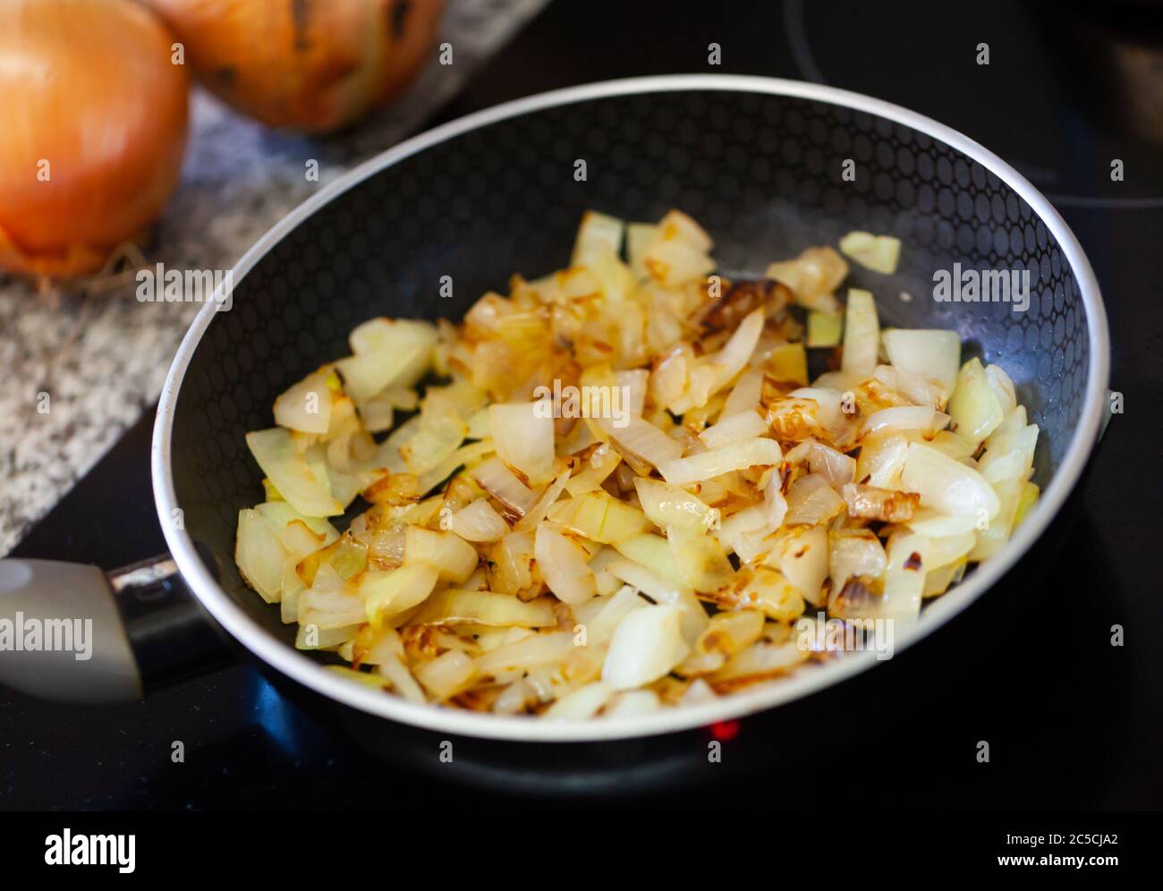 Poêle antiadhésive avec oignon en tranches sur une table de cuisson à ...