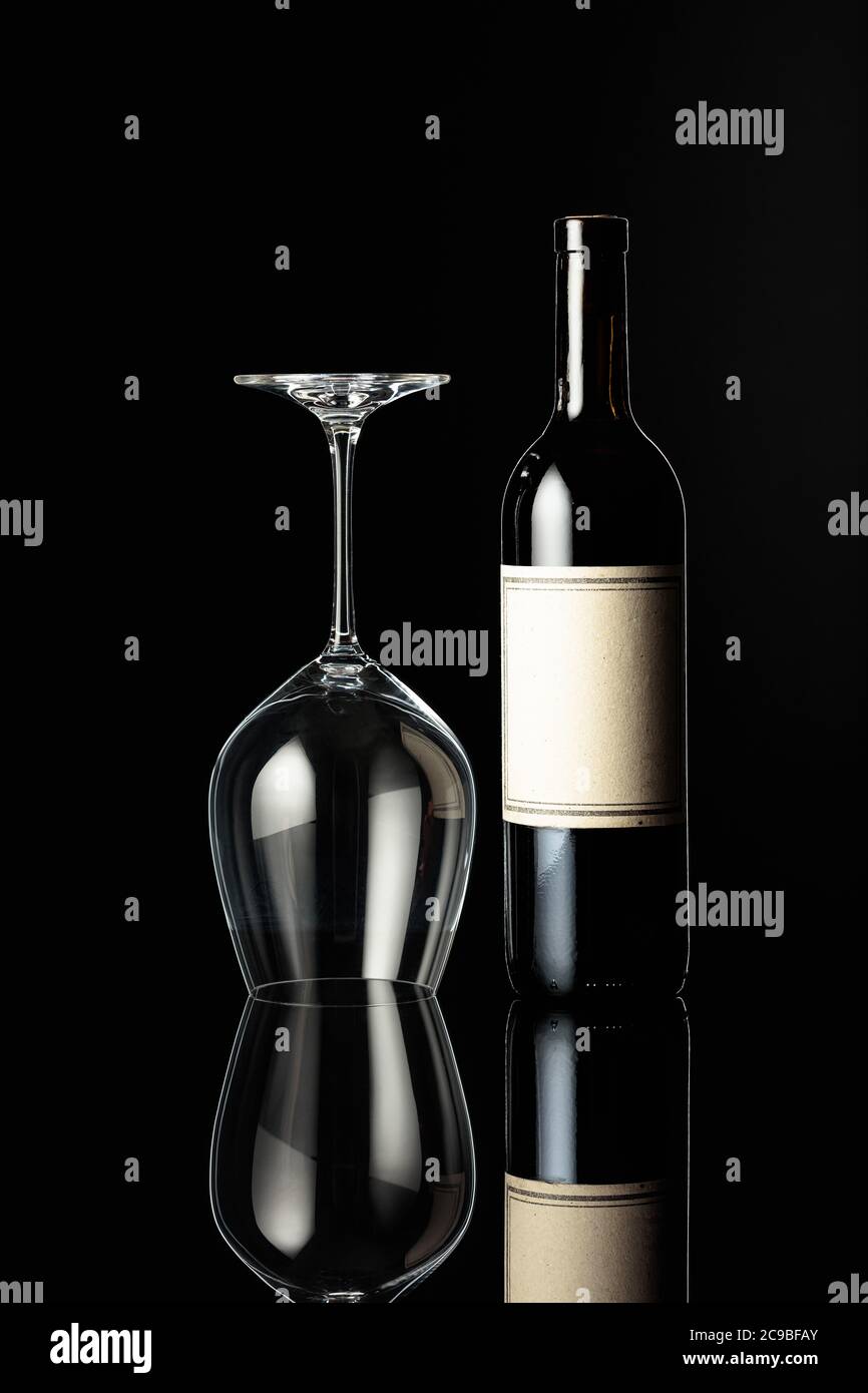 Bouteille de vin rouge et verre à vin inversé sur fond noir. Il y a une ...