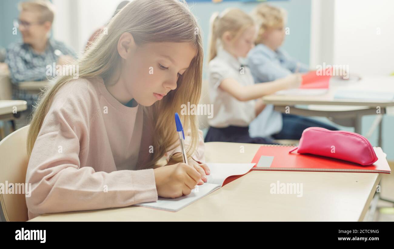 Dans la classe de l'école élémentaire, la fille caucasienne écrit dans ...
