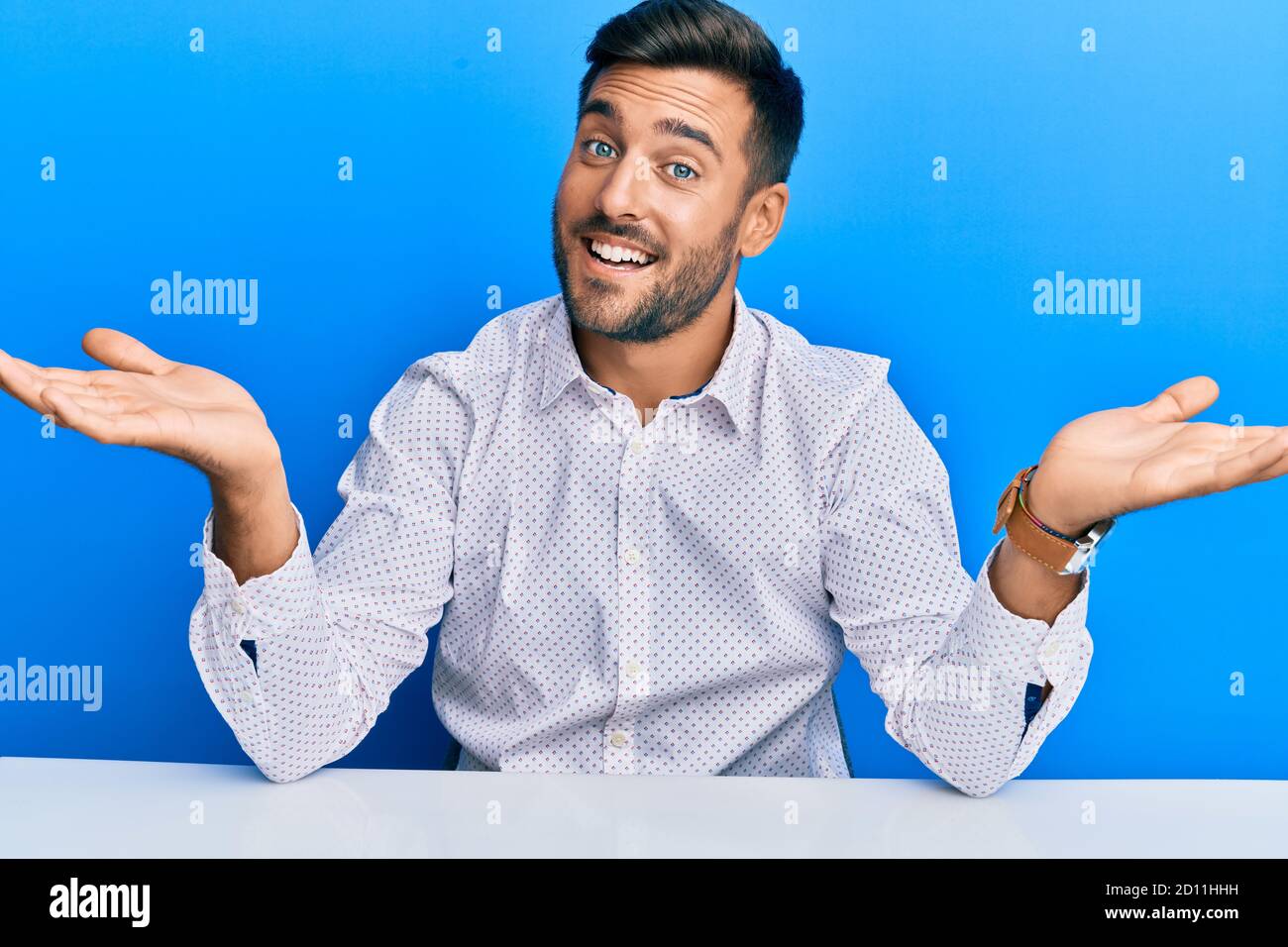 Beau hispanique homme portant des vêtements d'affaires assis sur la table souriant montrant les ...
