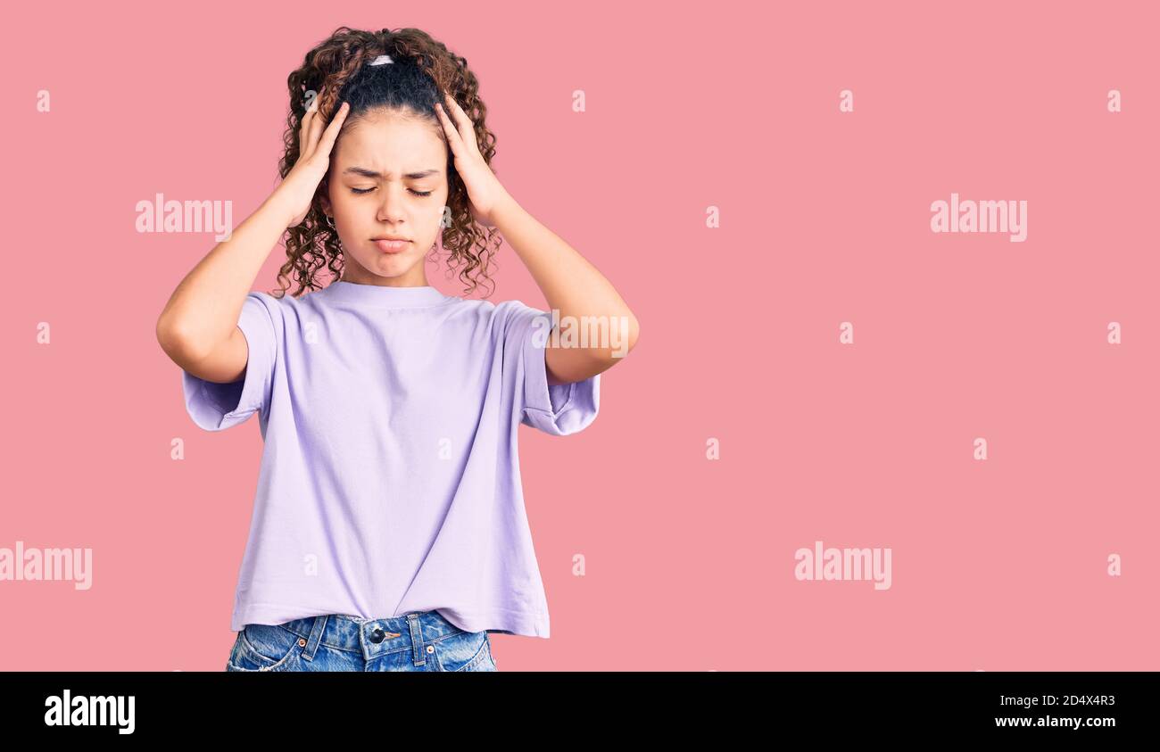 Belle fille de jeune fille avec des cheveux bouclés portant des vêtements décontractés souffrant ...