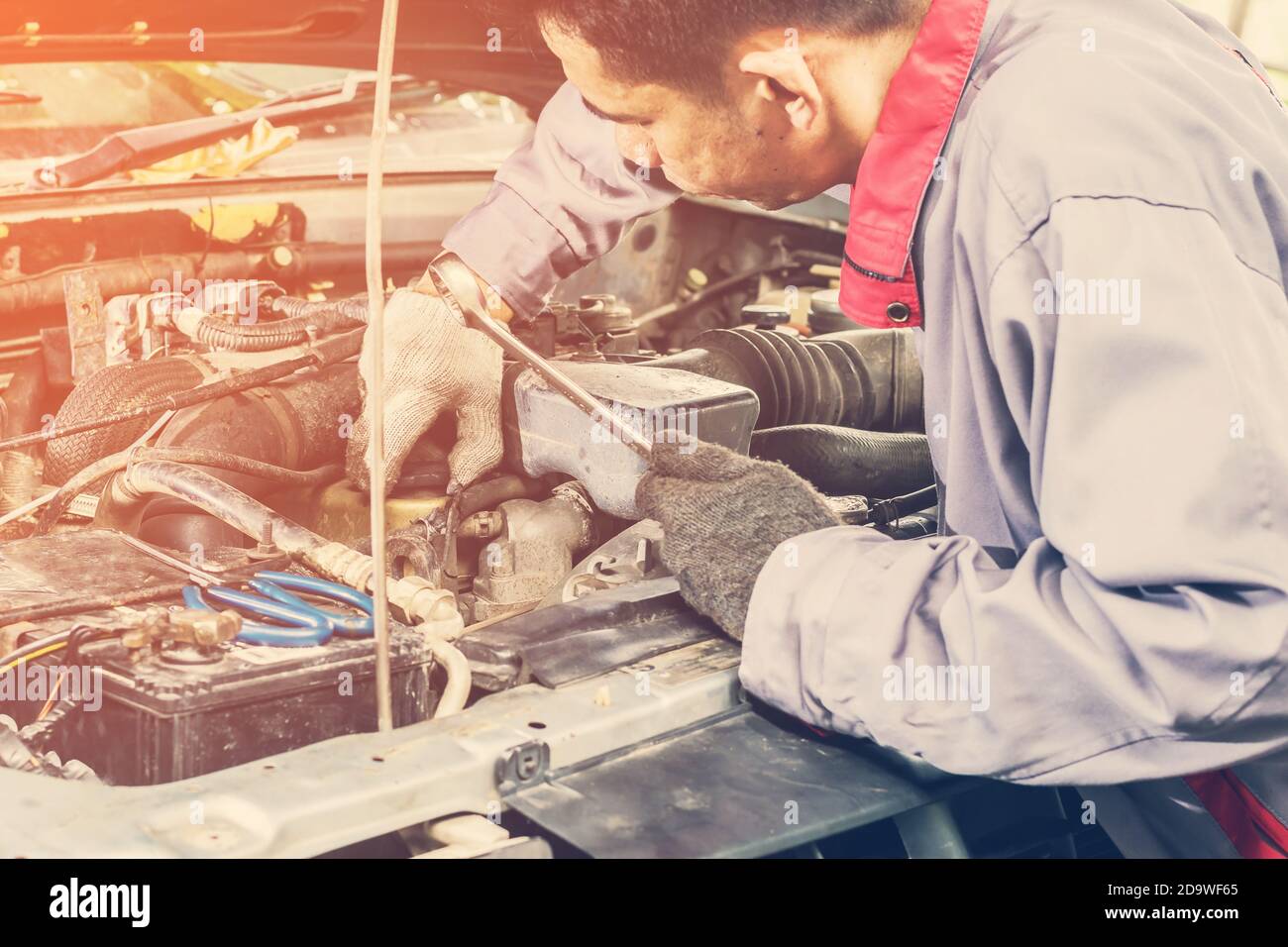 Le mécanicien de voiture en uniforme gris utilise un écrou de clé au moteur de la voiture pour l ...
