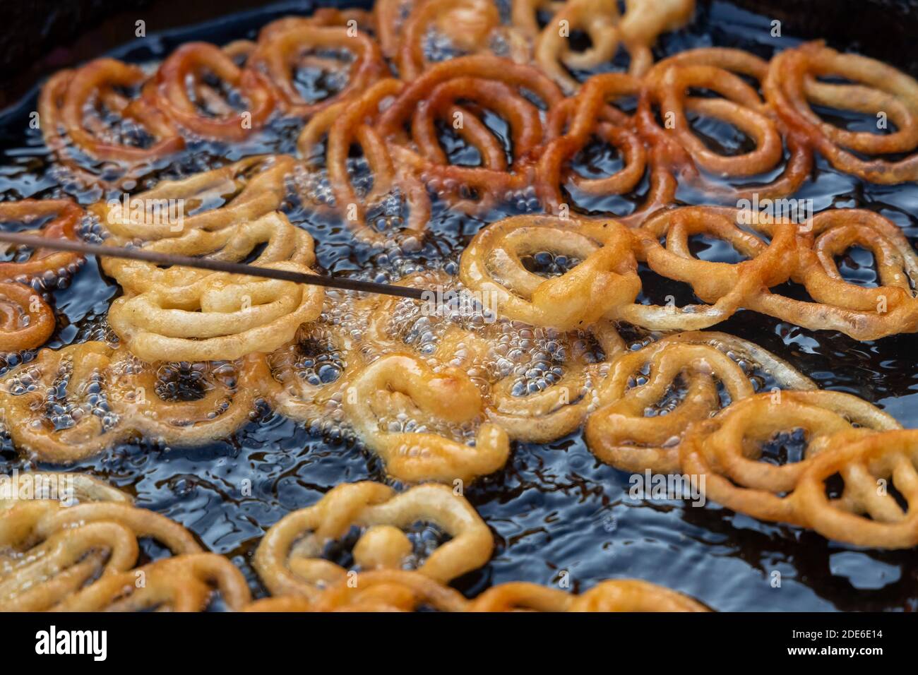 Faire frire de la pâte Jalebi dans de l'huile. La pâte rouge et orange ...