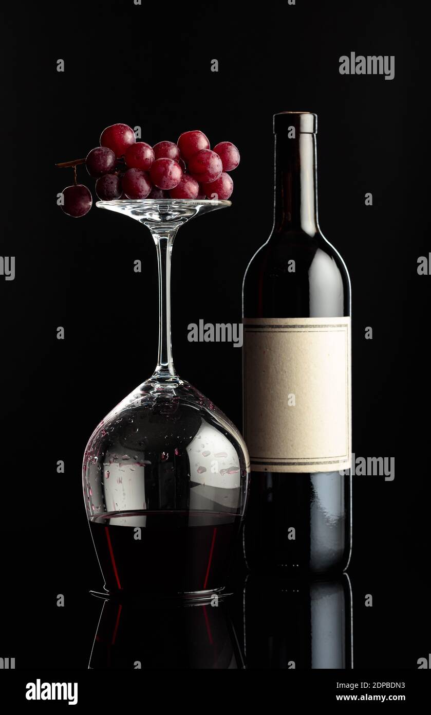 Bouteille de vin rouge et verre à vin inversé avec vin sur fond noir ...
