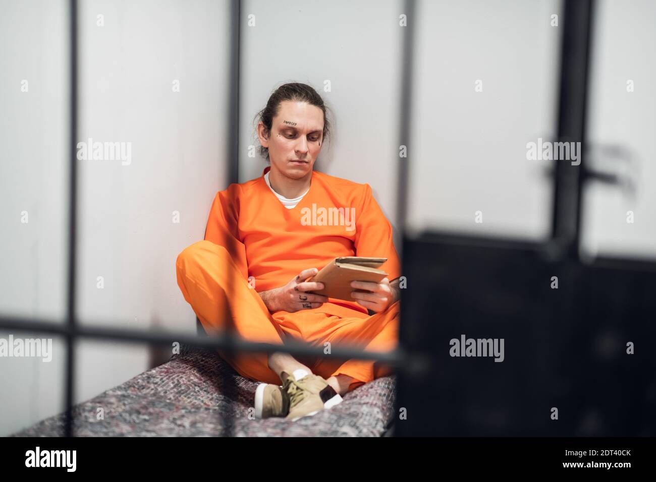 Un jeune criminel dans une cellule solitaire lit un livre assis sur un ...