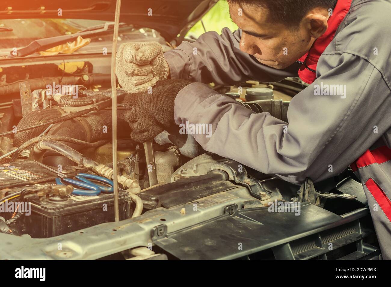 Le mécanicien de voiture en uniforme gris utilise un écrou de clé au moteur de la voiture pour l ...