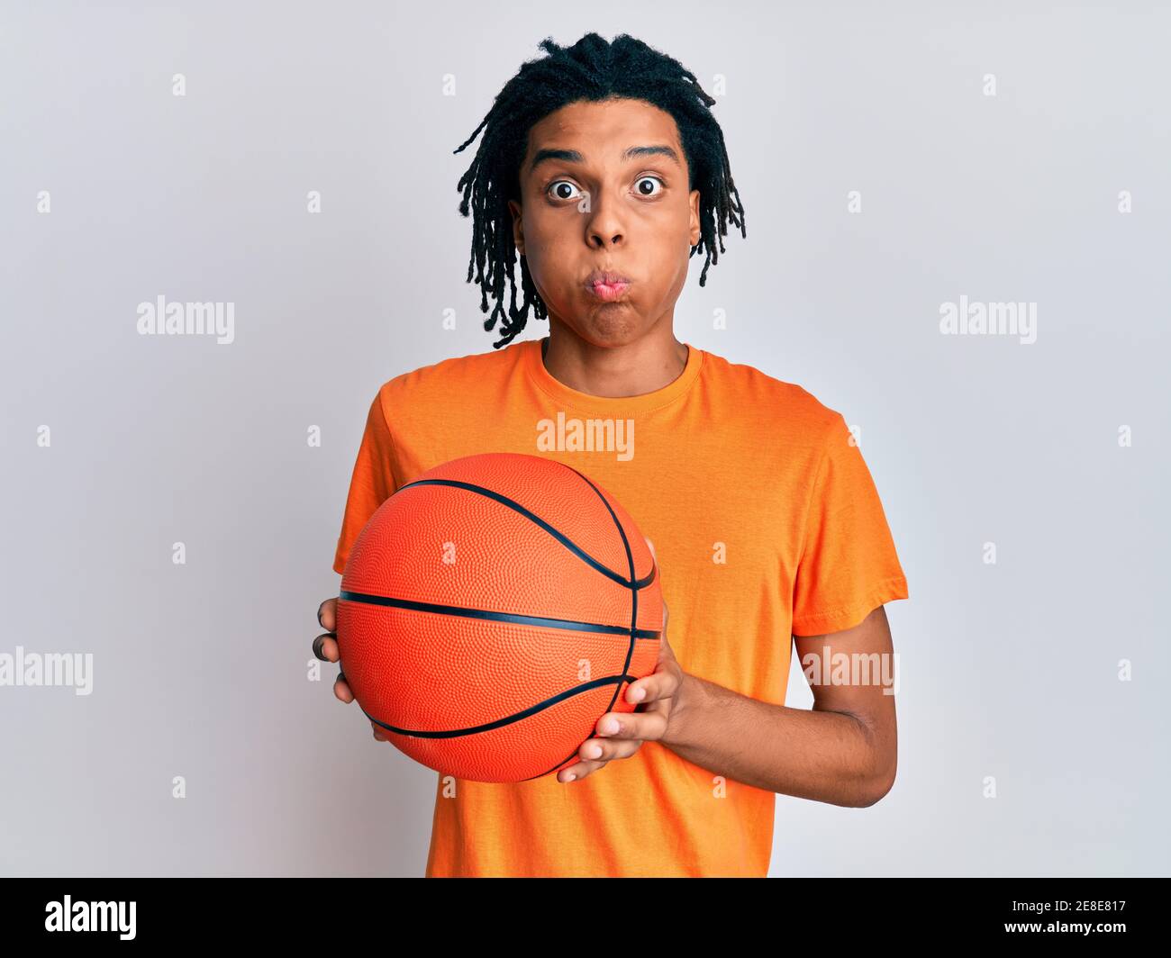 Jeune afro-américain tenant le ballon de basket-ball puffant les joues ...