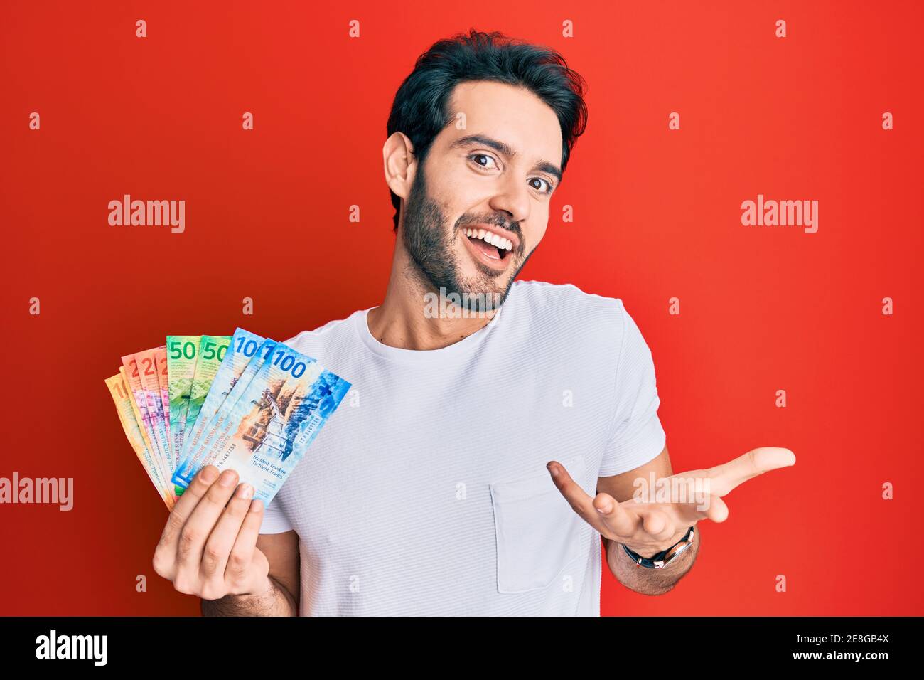 Jeune hispanique détenant des billets en francs suisses célébrant sa réussite sourire heureux et ...