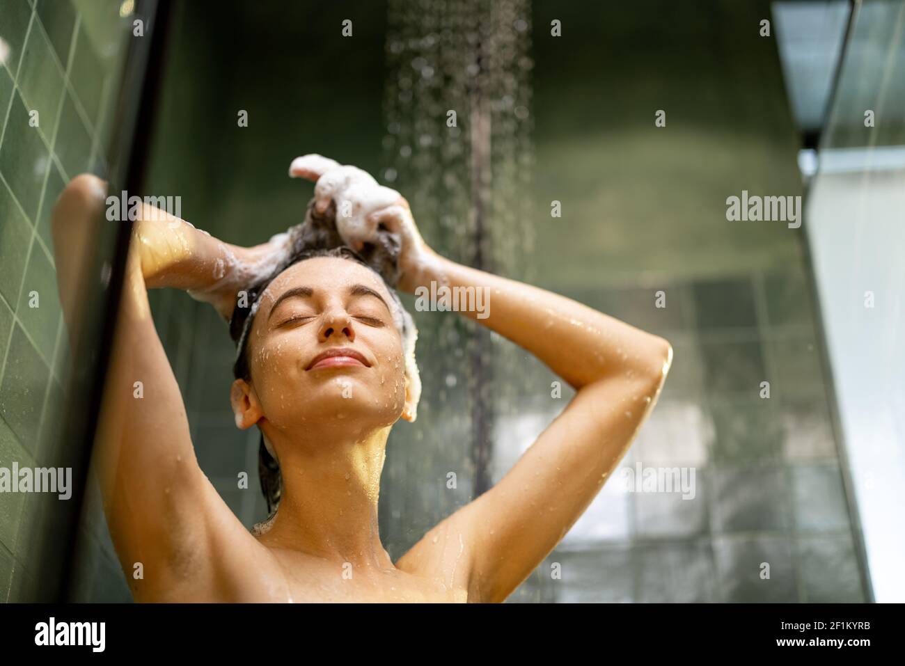 Bonne femme avec les yeux fermés dans la douche rincer shampooing avec ...