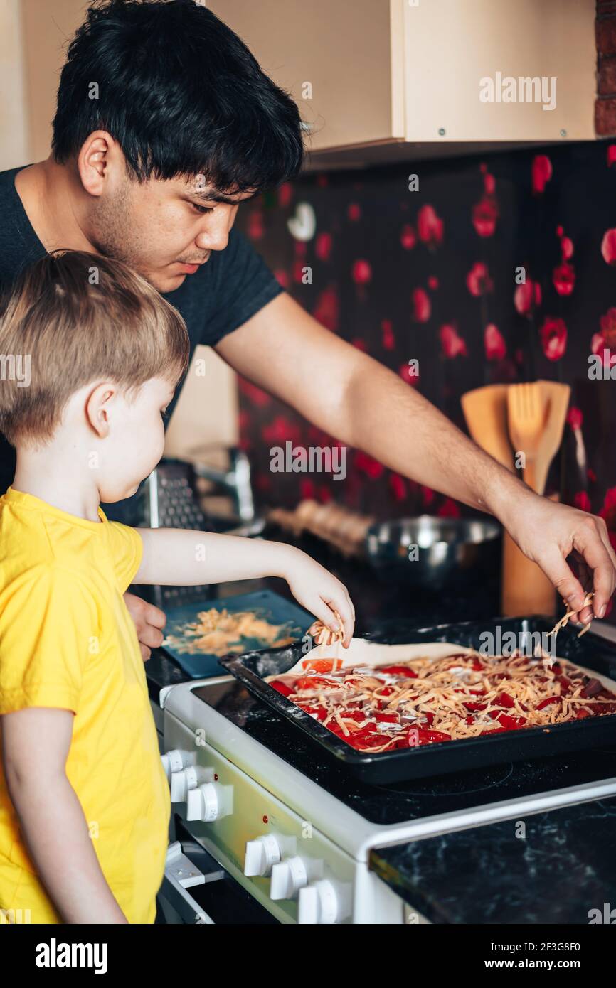 Père et fils saupoudrer de fromage râpé sur la pizza. Préparation pour ...