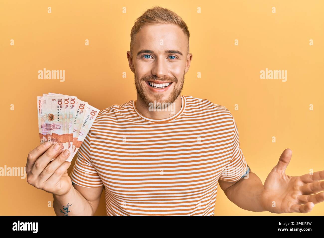 Jeune homme caucasien détenant 10 pesos colombiens célébrant la réussite sourire heureux et ...