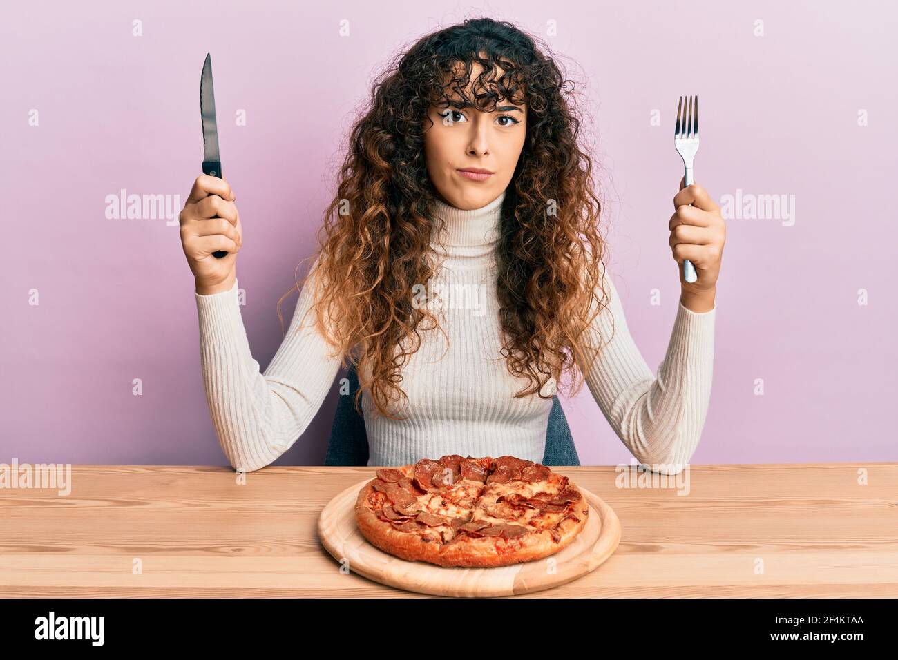 Jeune fille hispanique manger savoureux pepperoni pizza sceptique et ...