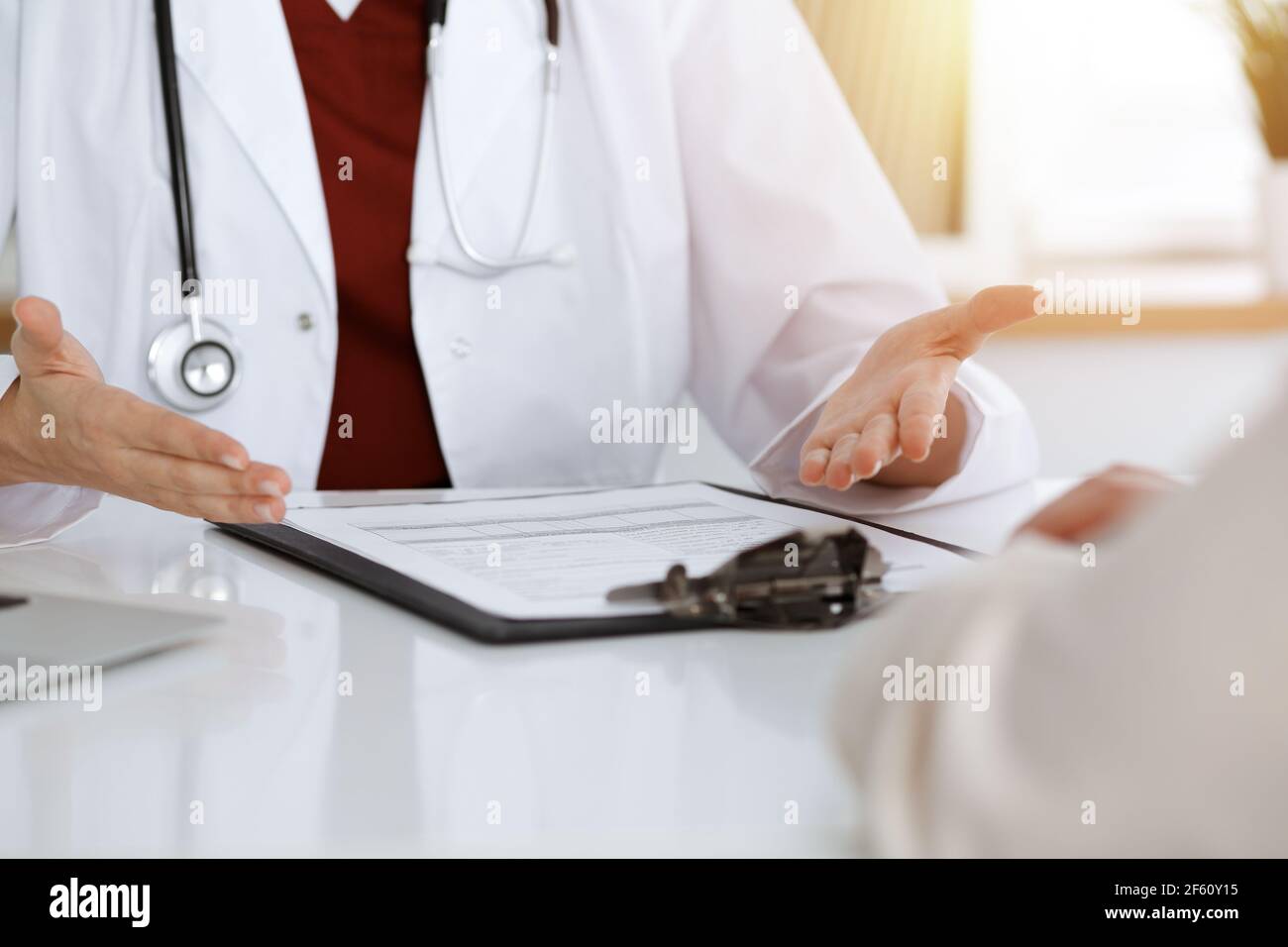 Femme-médecin et patient inconnu discutant quelque chose en étant assis ...