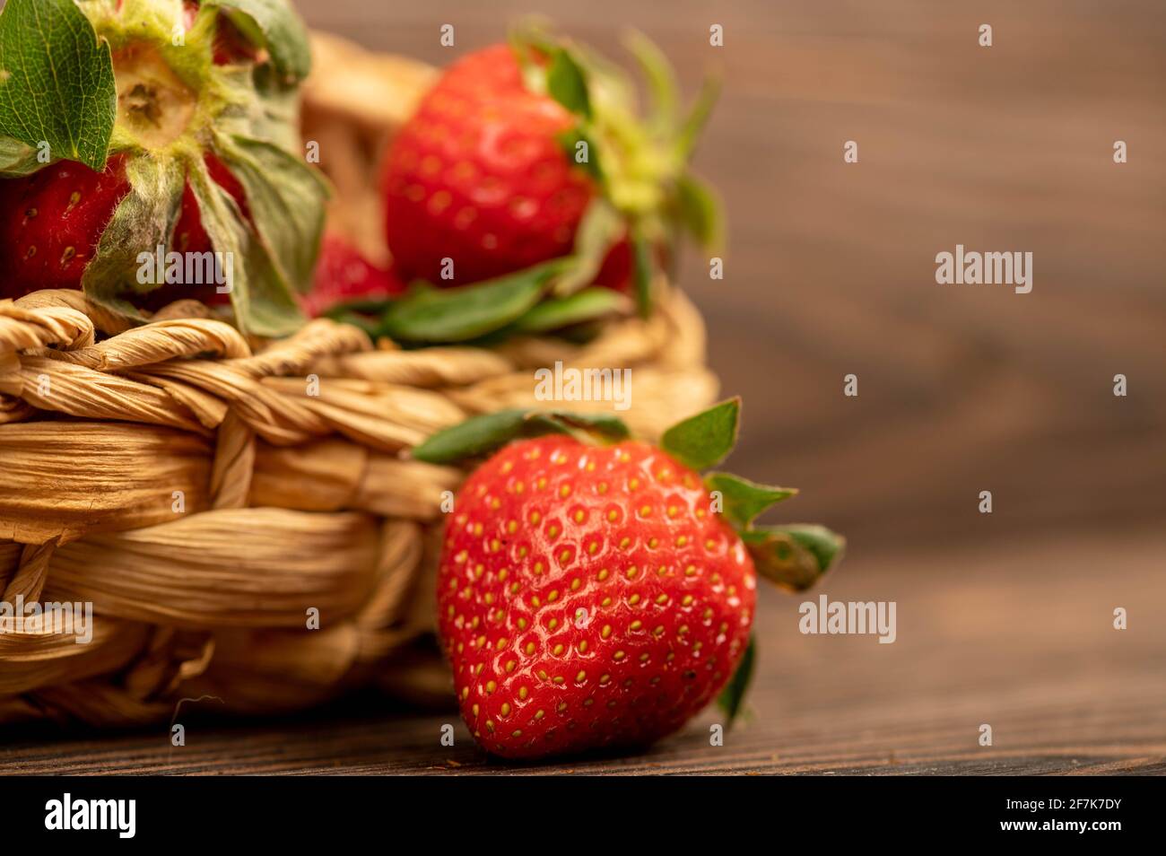 Fraises rouges fraîches dans un panier en osier sur une table en bois ...
