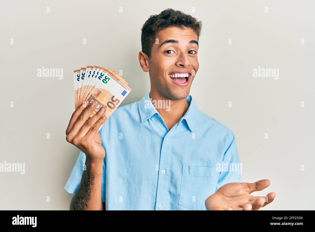 Un jeune homme afro-américain charmant détient une bande de 50 euros billets célébrant la ...