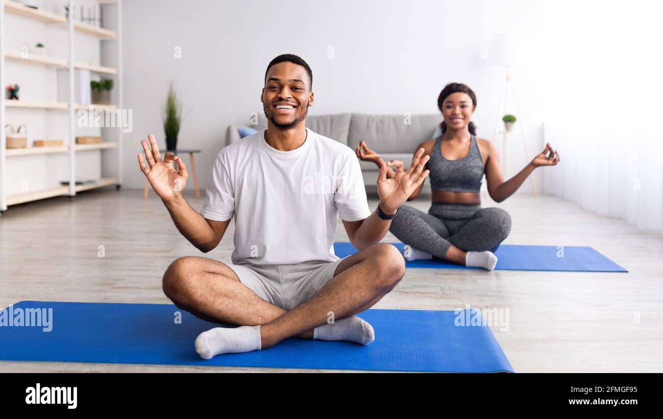 Joyeux homme noir faisant la pratique du yoga avec sa petite amie ...