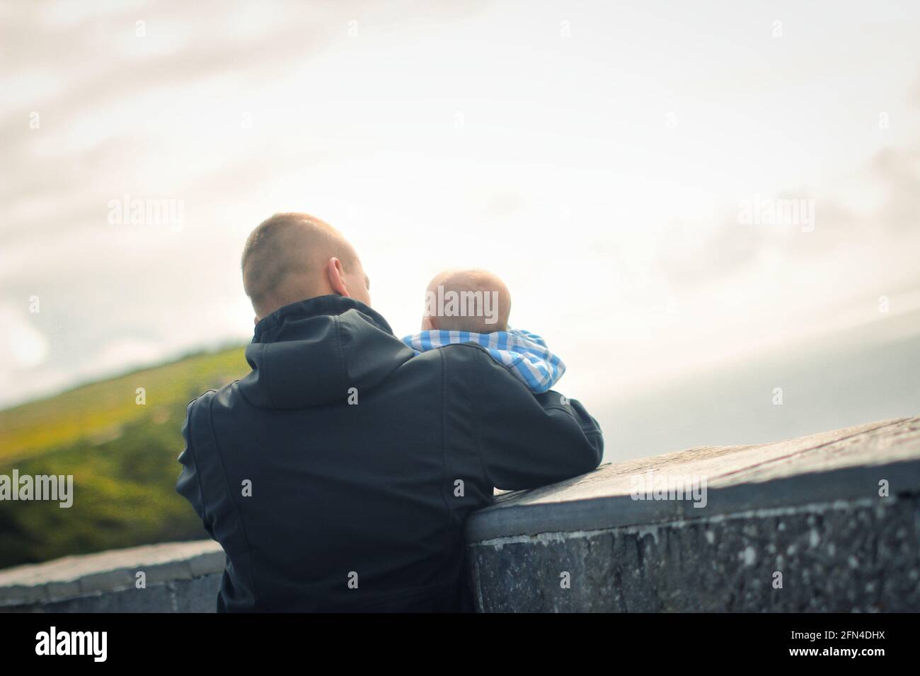 L'homme tient son nouveau-né devant un coucher de soleil sur la mer ...